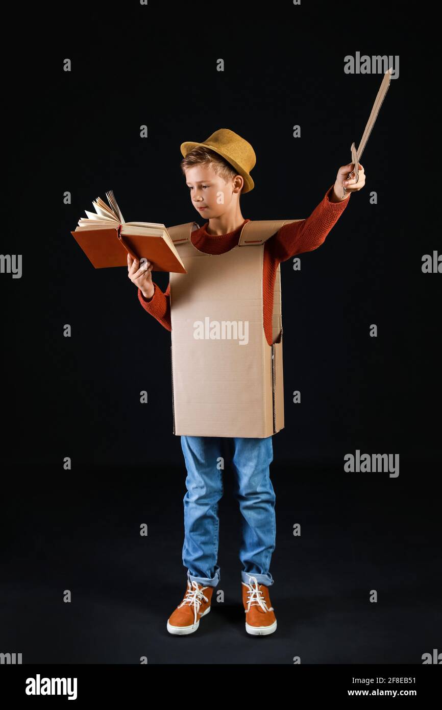 Cute little boy dressed as knight holding book on dark background Stock ...