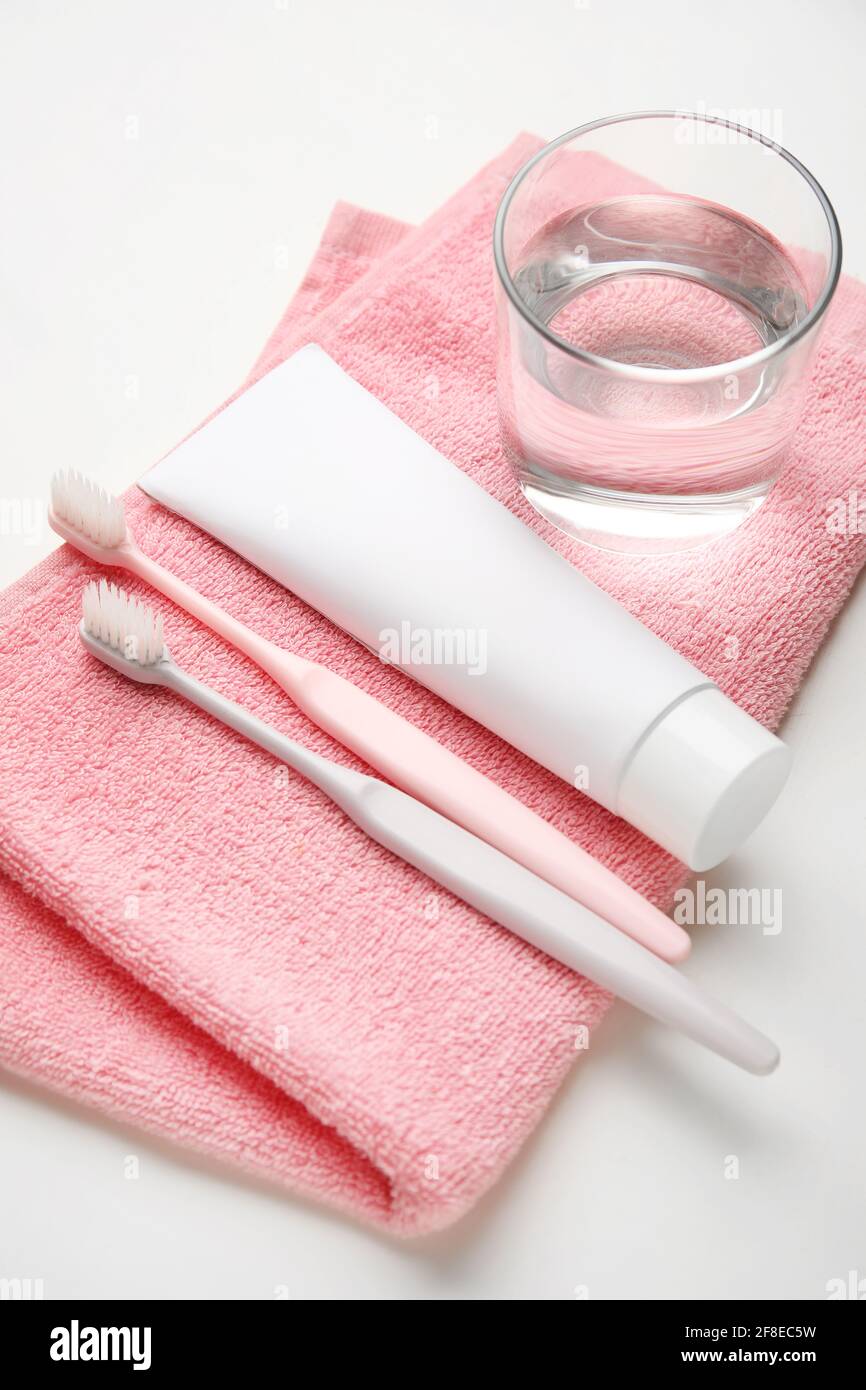 Tooth brushes, paste, glass of water and towel on white background ...