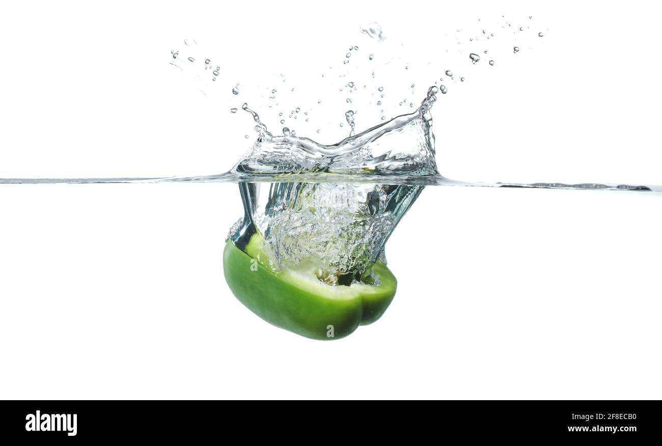 Falling of fresh cut bell pepper into water against white background ...
