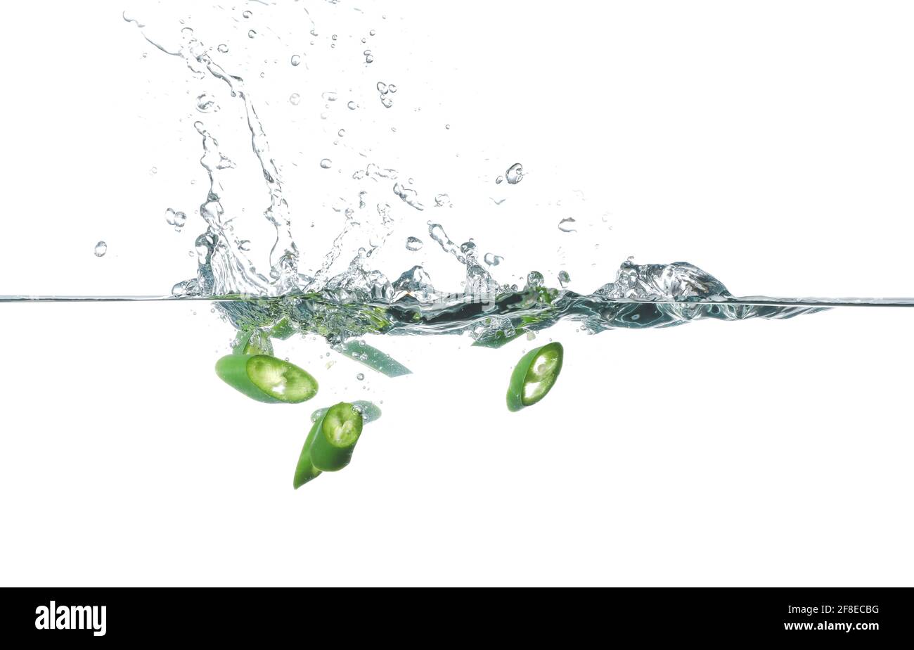 Falling of fresh cut chili pepper into water against white background ...