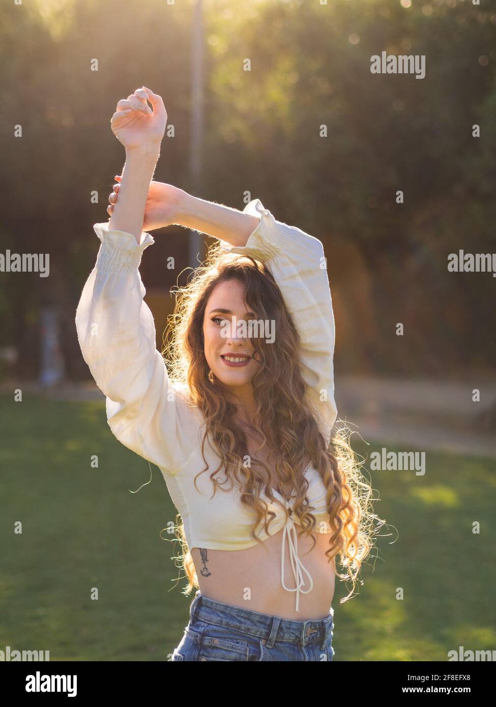 Pretty long-haired Spanish girl enjoying the spring weather; a model is posing with her arms up ...