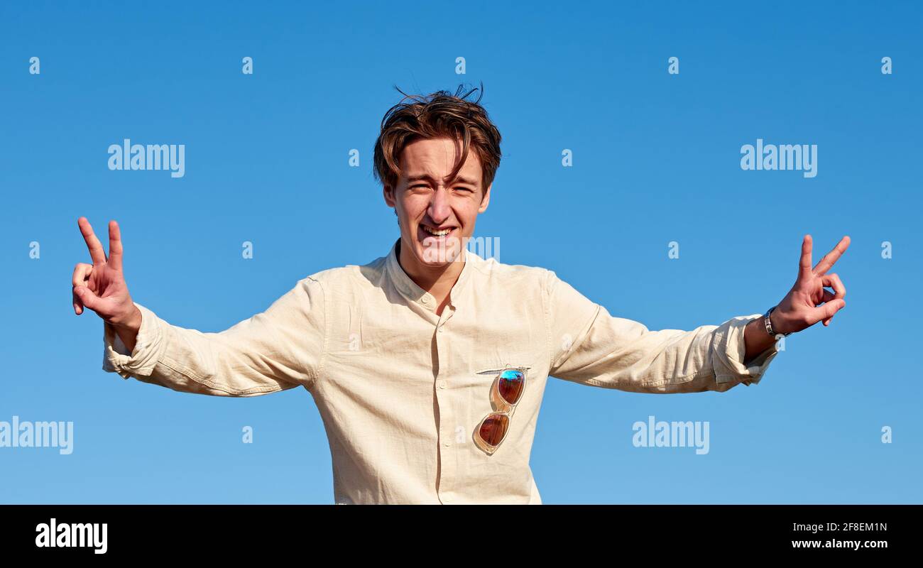 Cheerful young Spanish handsome male showing the peace sign against the ...