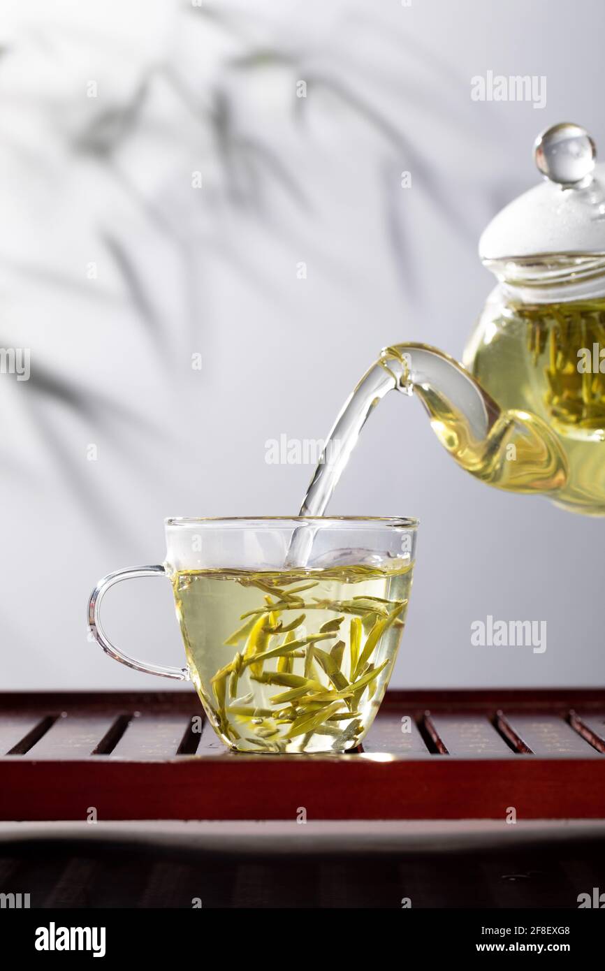 Vertical shot of green tea pouring from a glass pot into a cup with a ...