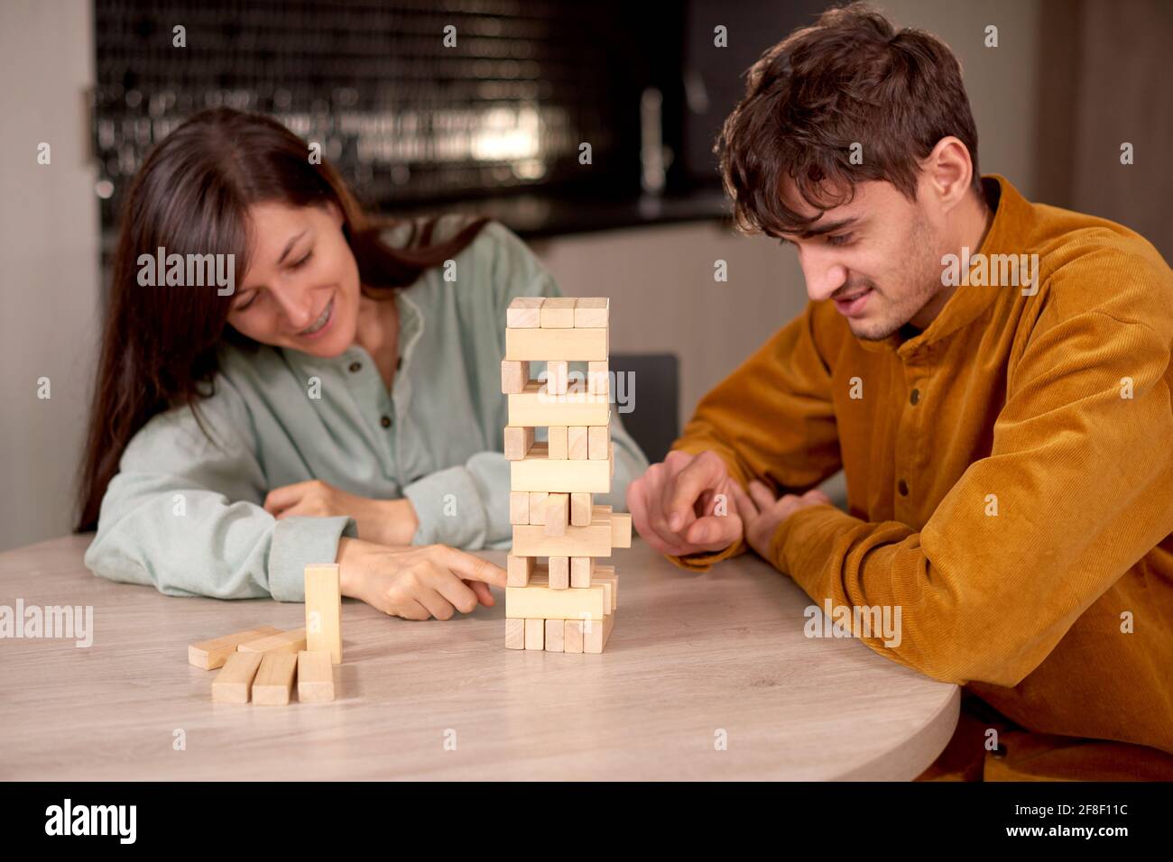 Happy couple playing Jenga while sitting in kitchen at home, having fun ...