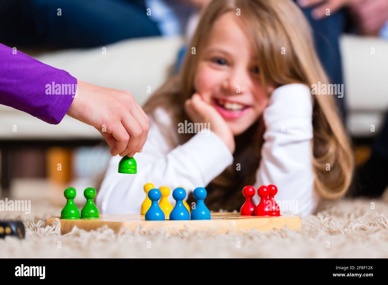Family playing board game ludo at home on the floor, focus on the arm ...