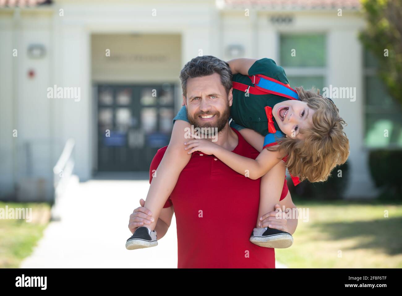 Teacher in t-shirt and cute schoolboy with backpack near school park ...