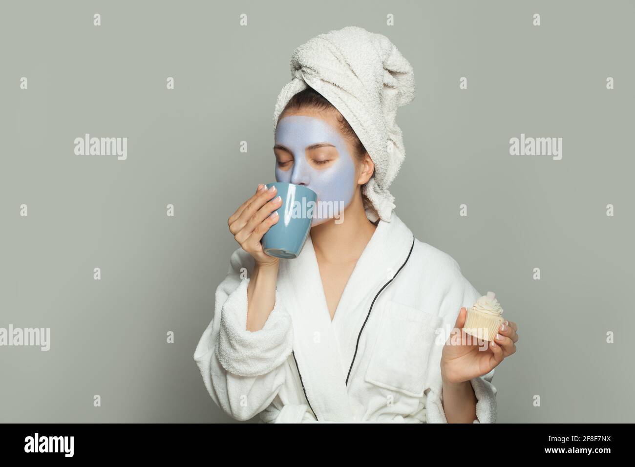 Attractive spa woman in cosmetic face mask eating breakfast and ...