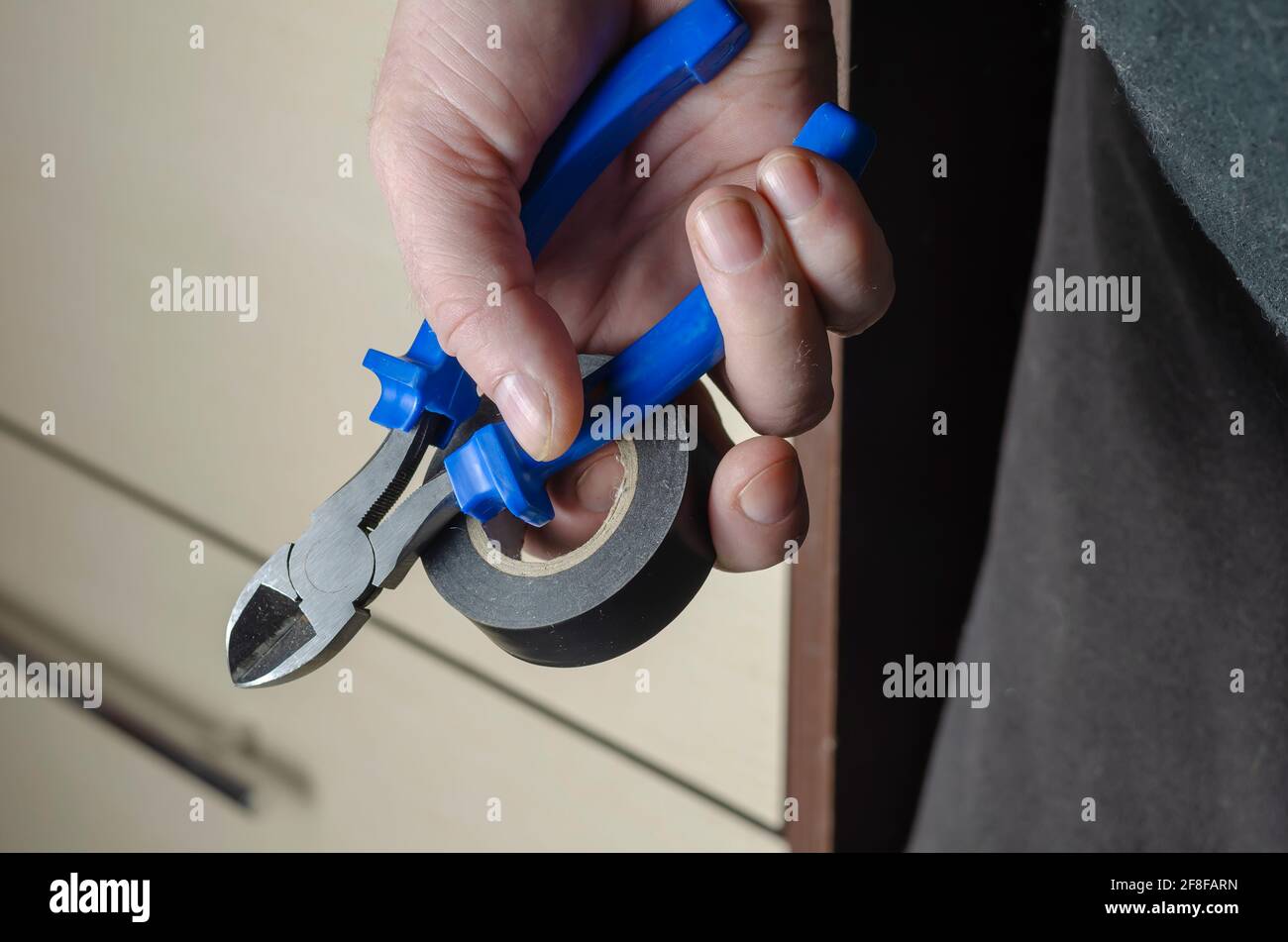 x®Man with side cutters and duct tape against a light brown cabinet ...