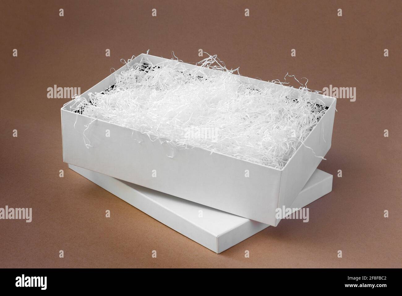 white shredded paper in a white open box on the lid on a paper beige ...
