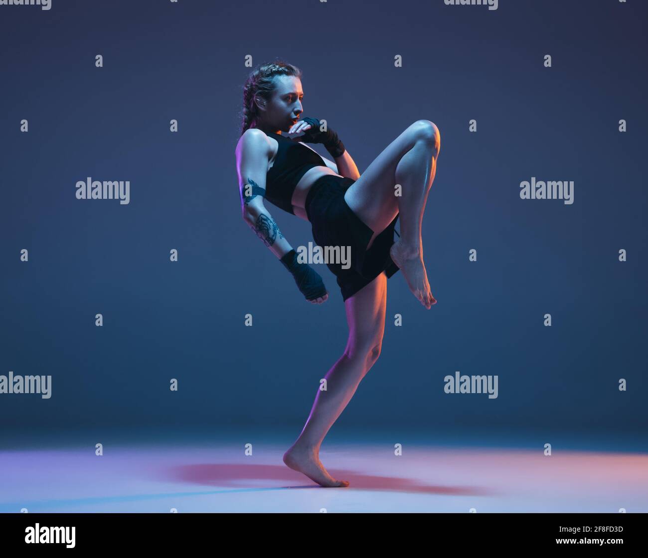 Young female MMA fighter posing isolated over blue background in neon ...
