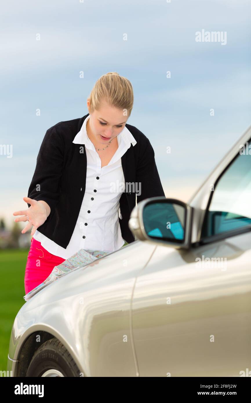 Young woman in front of bonnet of a car with map looking for directions ...