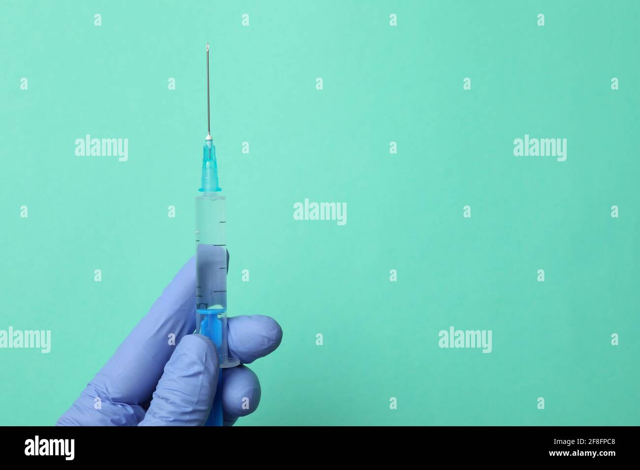 Hand in medical glove hold syringe on mint background Stock Photo - Alamy