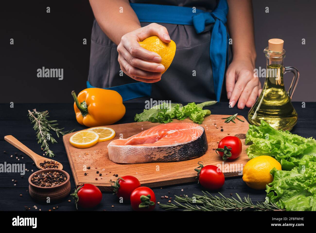 Female hands squeeze lemon juice on a salmon steak. Cooking process ...