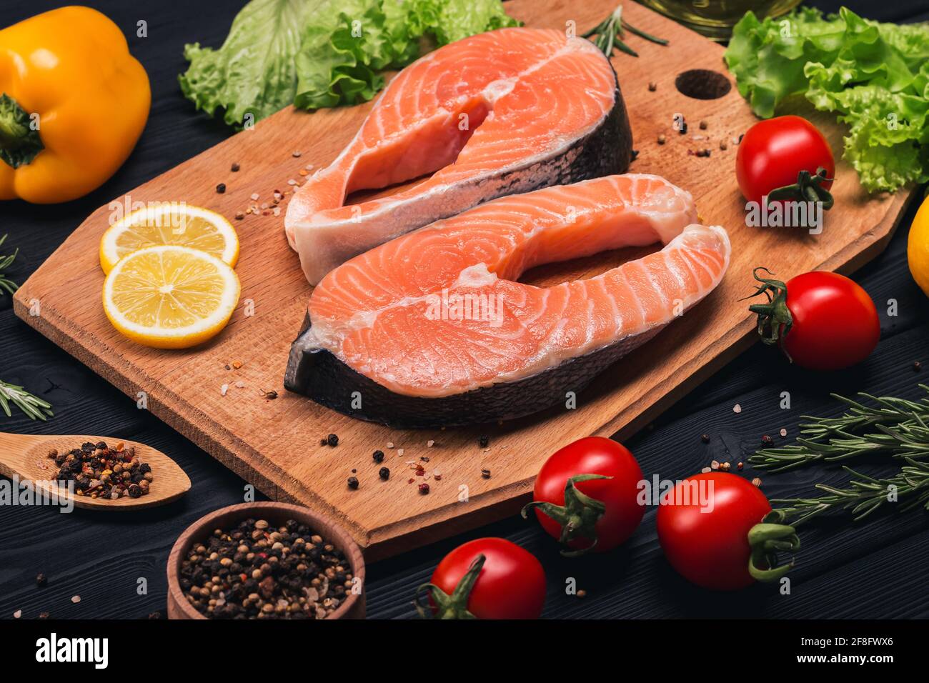 Two juicy appetizing salmon steaks are laid out on a wooden board next ...