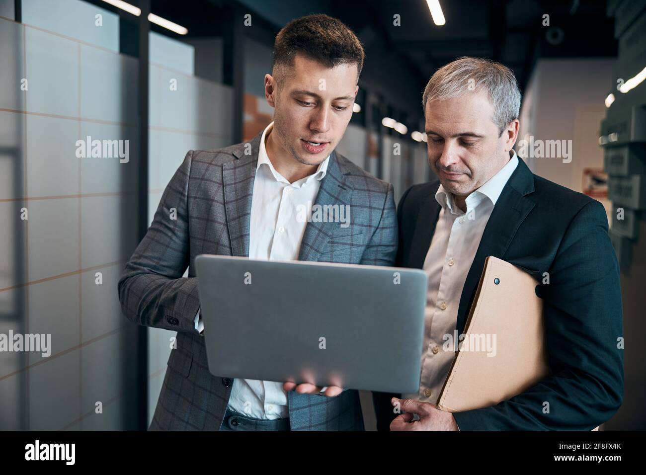 Business colleagues using notebook in office corridor Stock Photo - Alamy