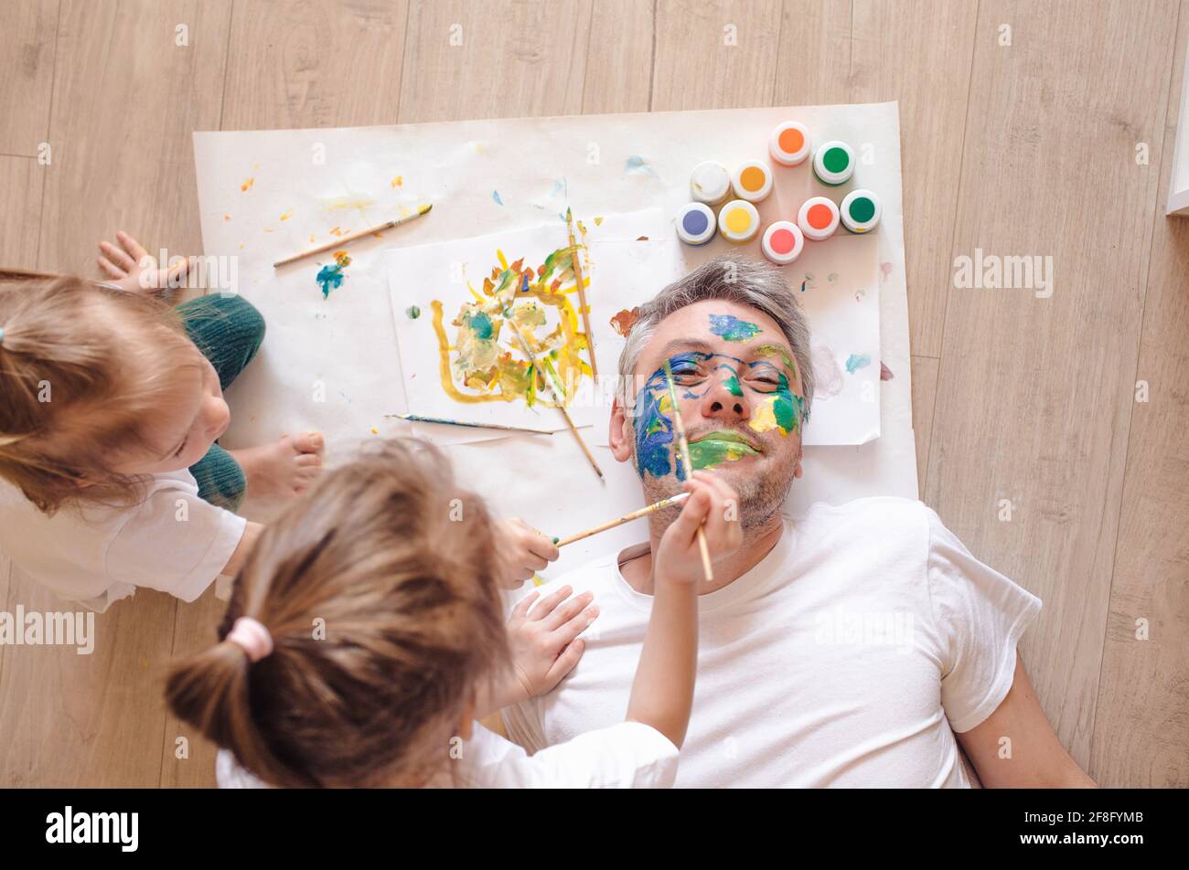 happy dad is lying on the floor, the children paint his face with ...
