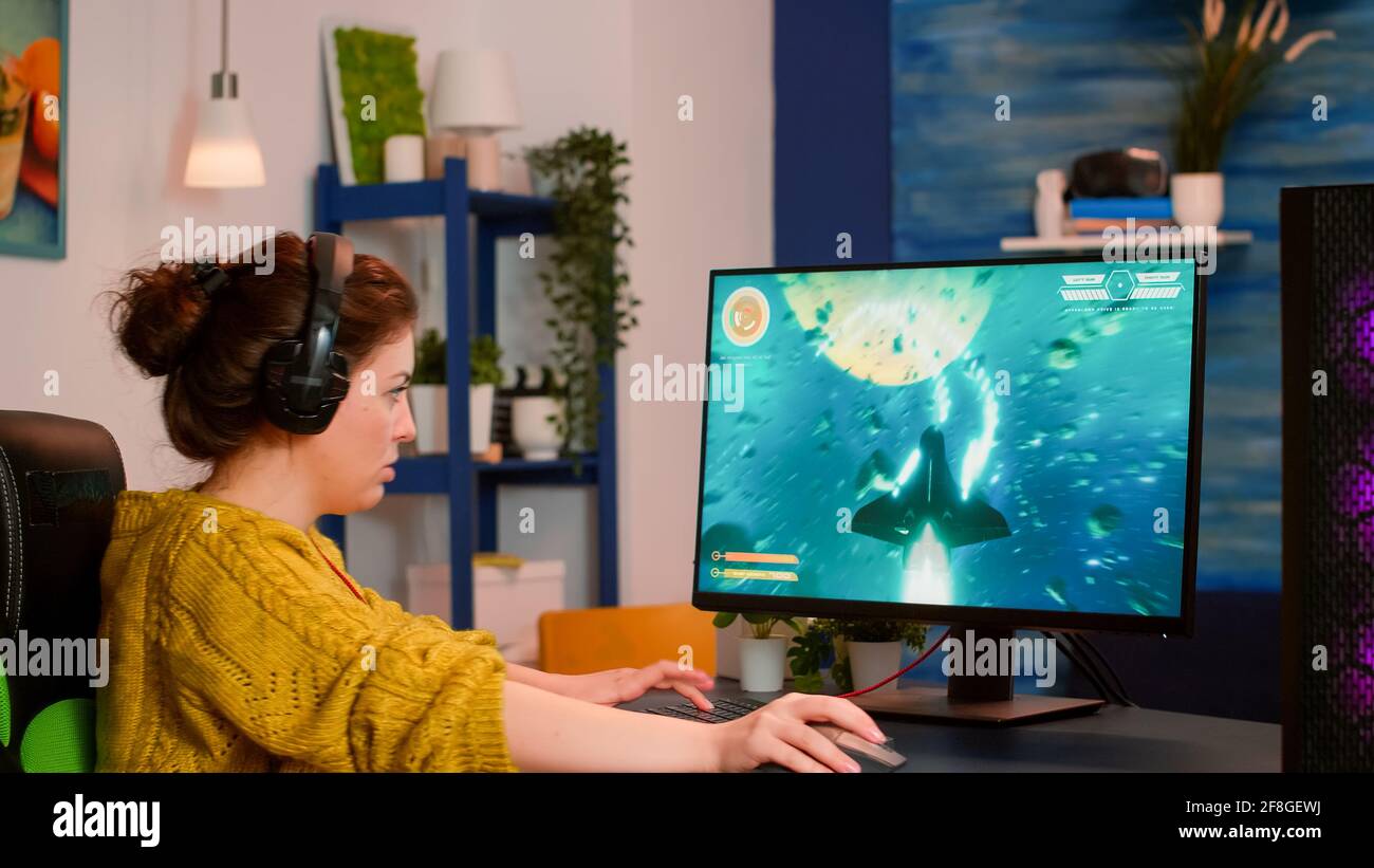 Gamer woman with headphones relaxing at home playing space shooter ...