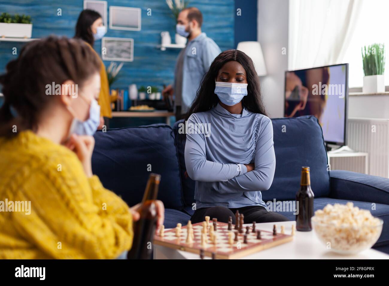 African woman wearing face mask playing chess drinking beer, keeping ...