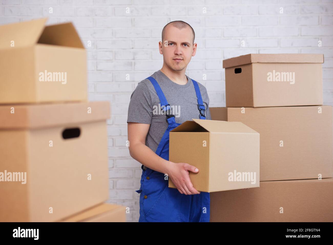 moving day or postal delivery concept - young man loader in warehouse ...