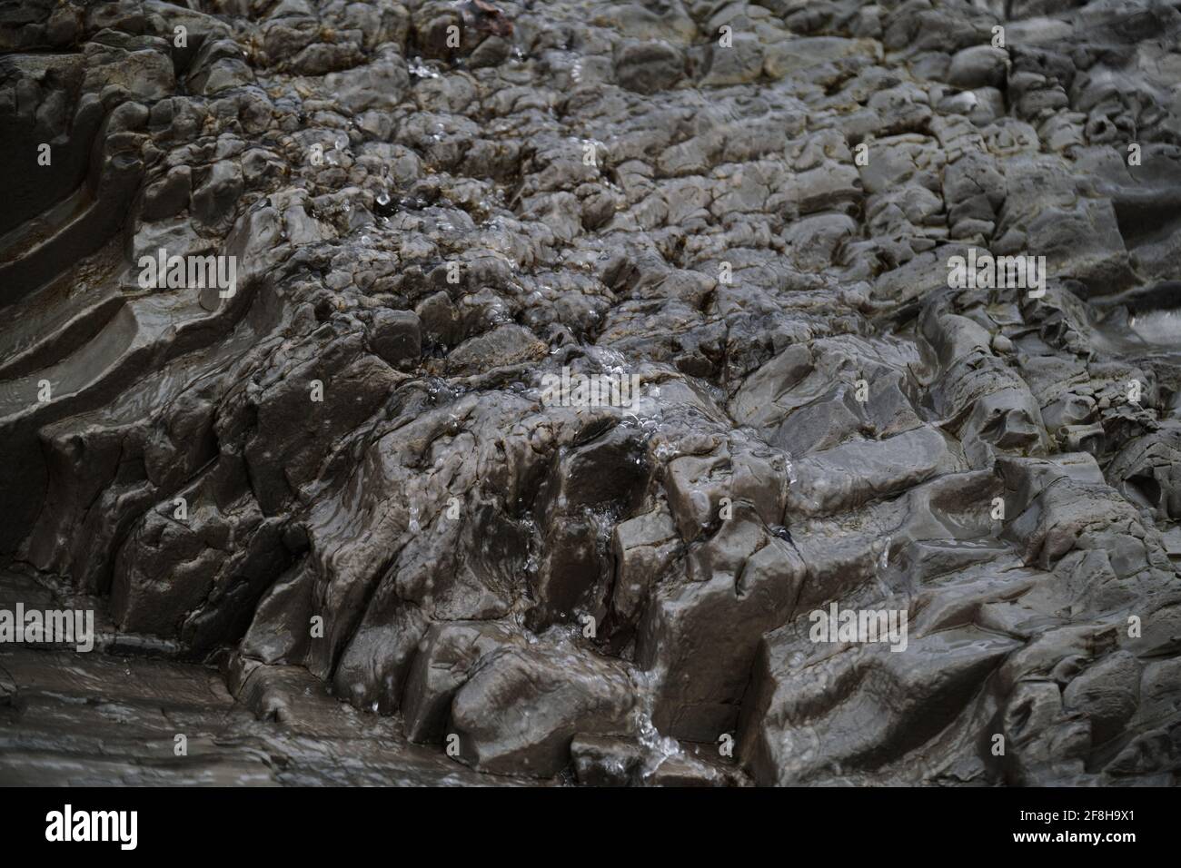Thin stream of water flows down gray textured rock. Natural natural ...
