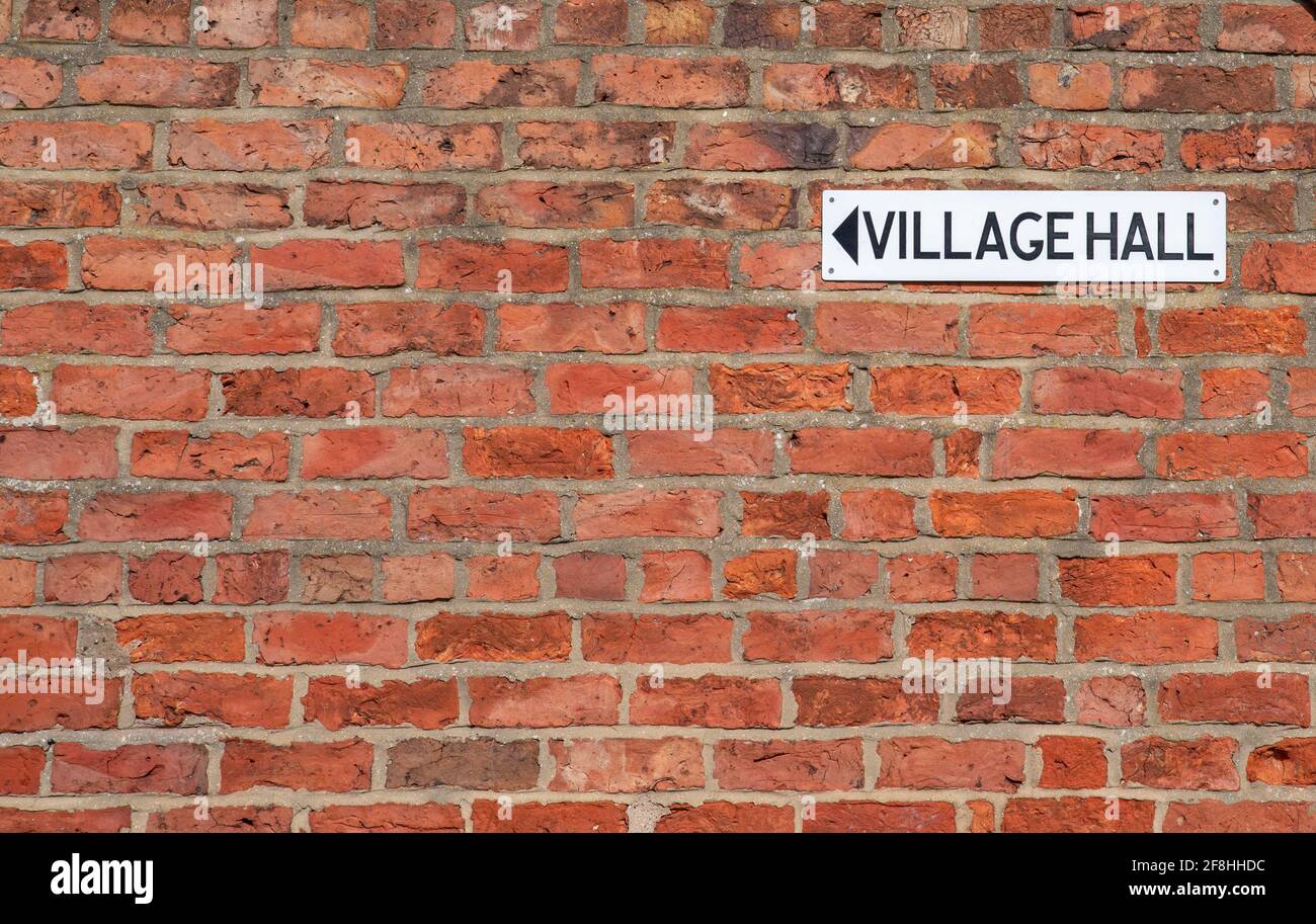 Small black and white Village Hall sign with arrow mounted on a red ...