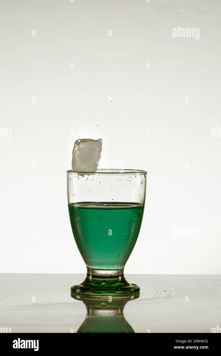 Ice cube falling into a glass of green drink isolated on the reflective surface Stock Photo - Alamy