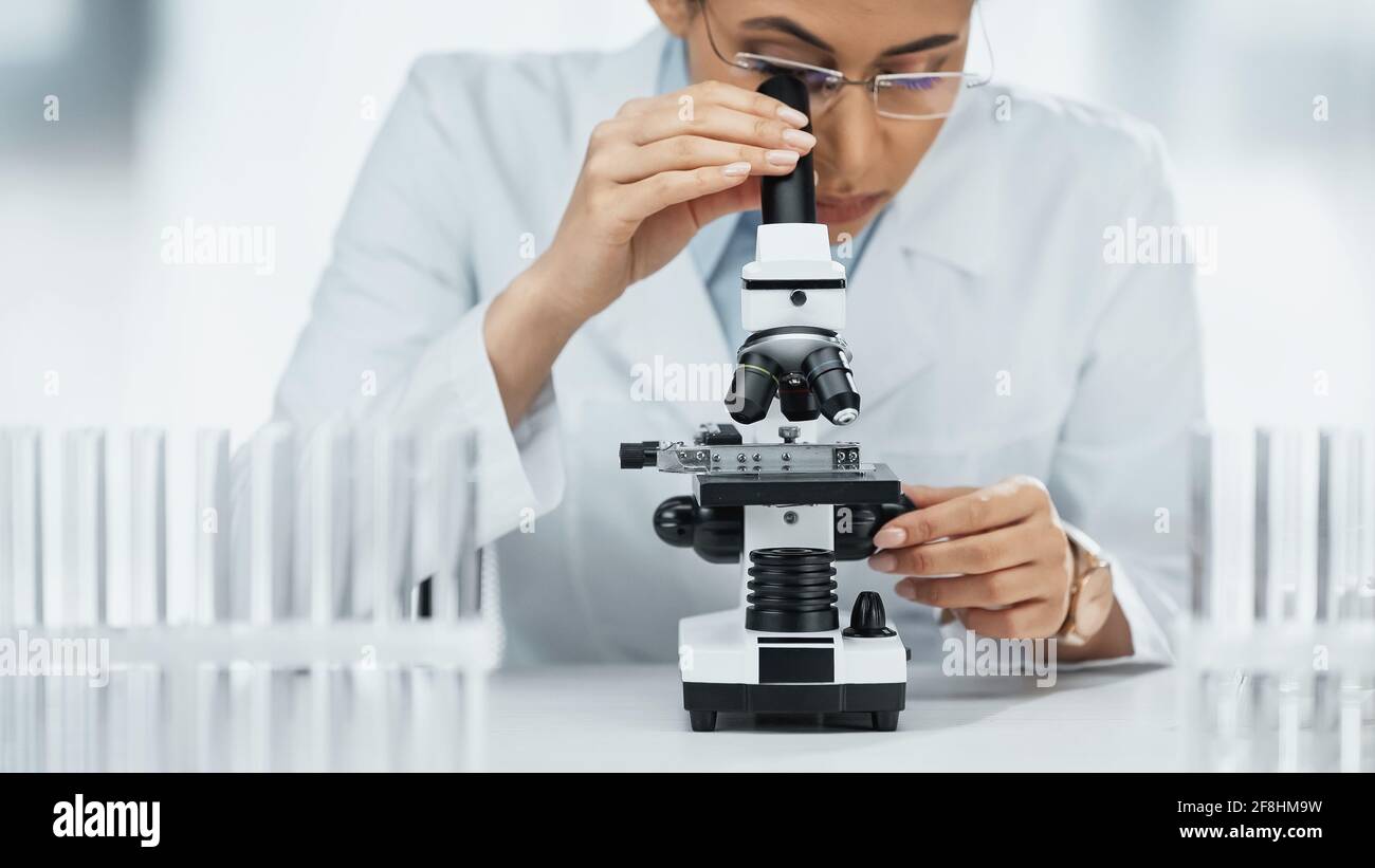 focused african american scientist looking through microscope near test ...