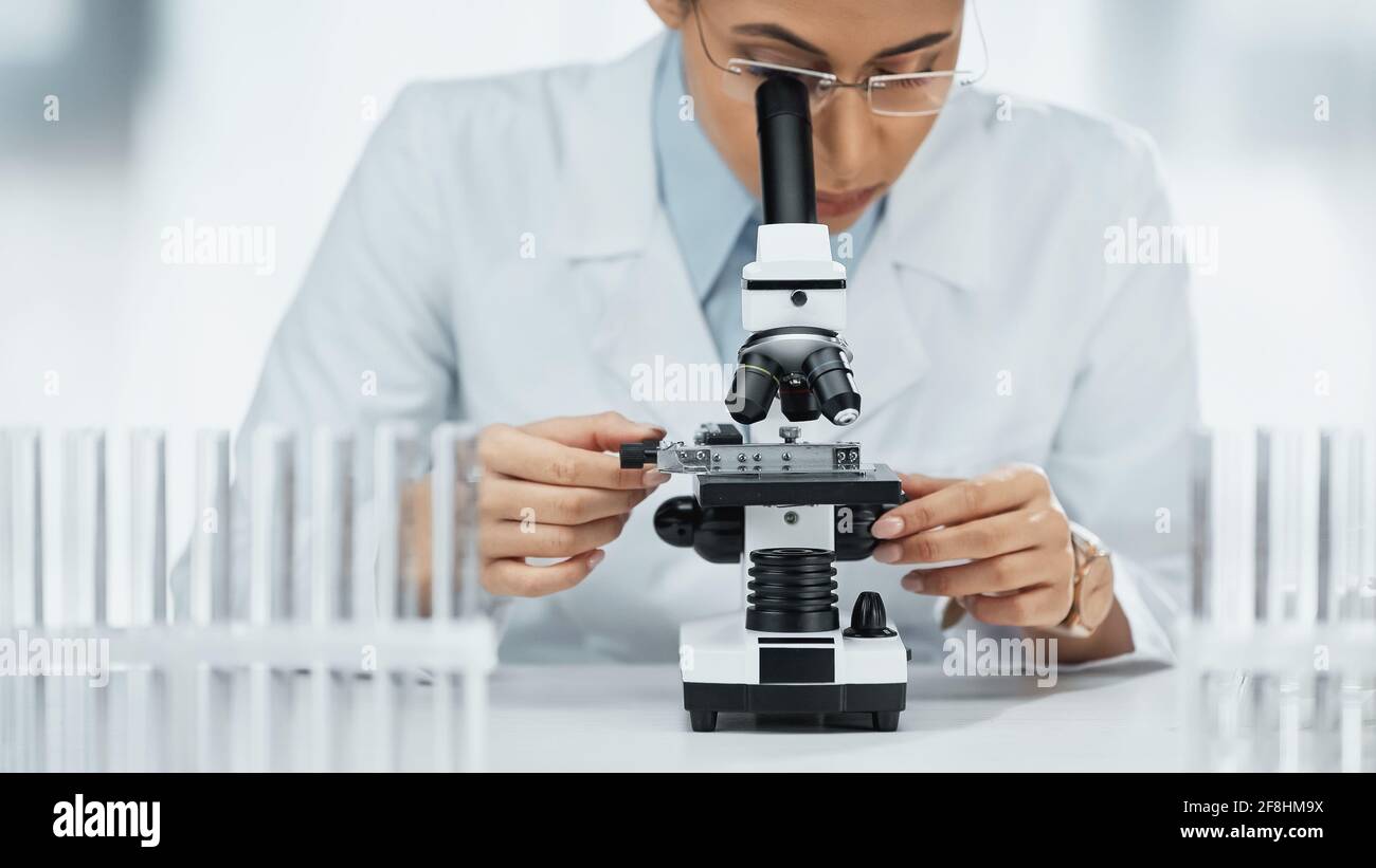 african american scientist looking through microscope near test tubes ...