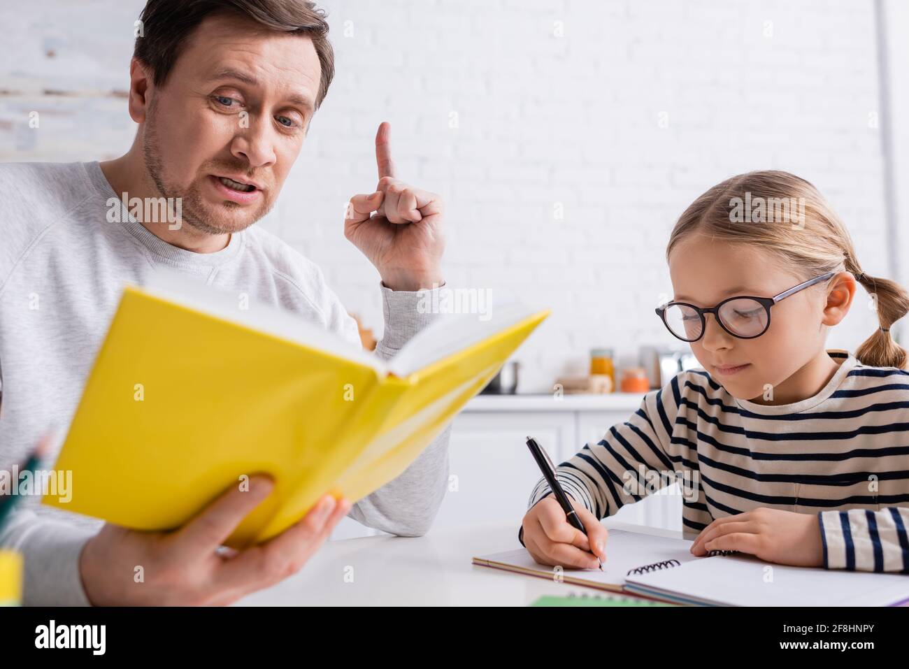 man reading book and showing attention gesture near daughter writing in ...