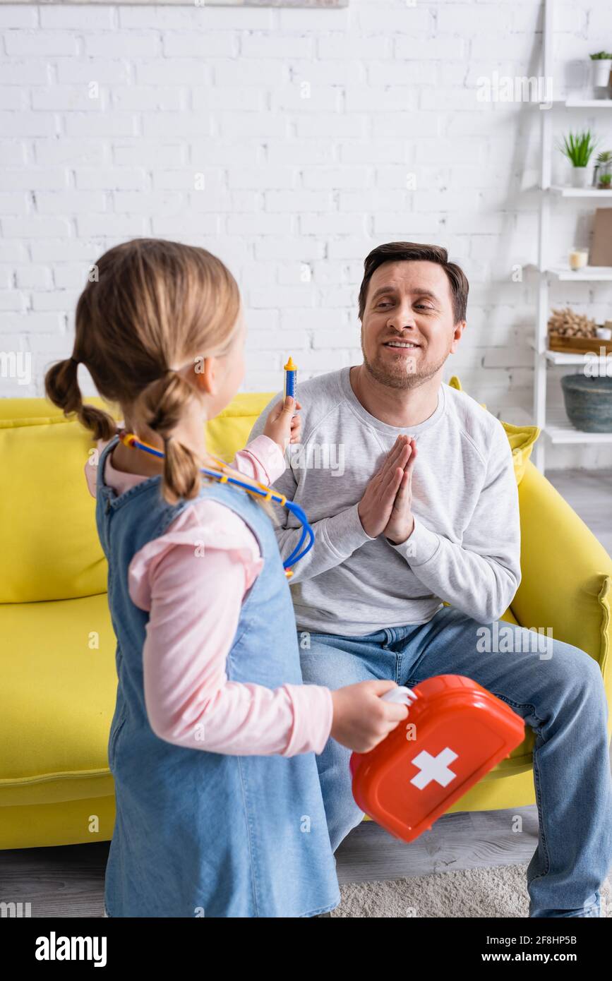 father showing please gesture near daughter holding toy syringe and ...