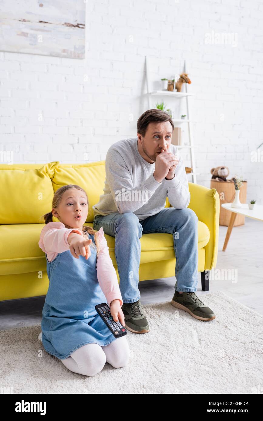 surprised girl pointing with finger while watching movie with father ...