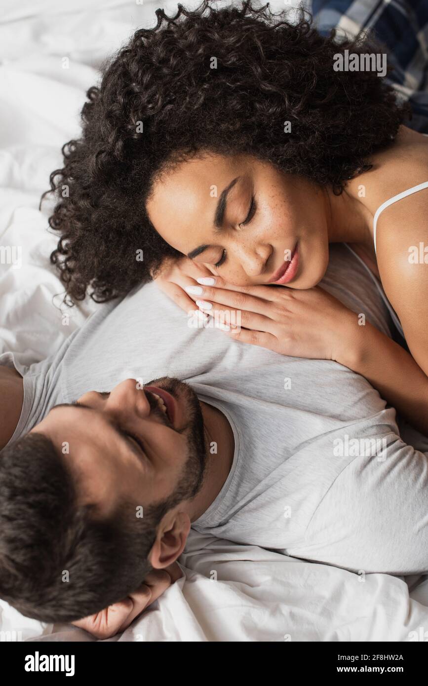 High Angle View Of Smiling Interracial Couple Lying Together On Bed