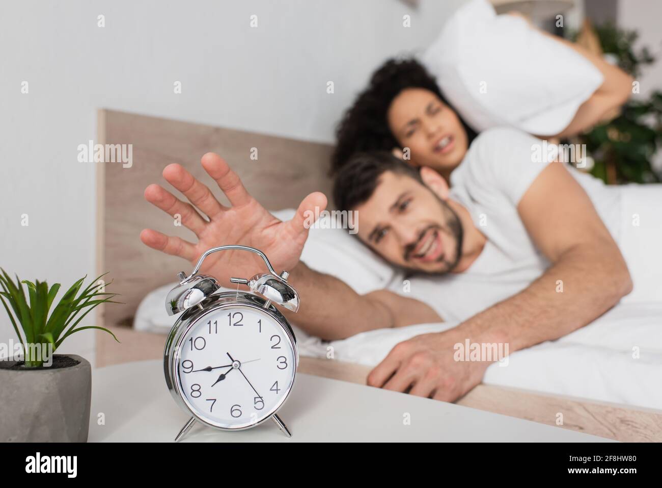 displeased man reaching alarm clock near african american girlfriend in ...