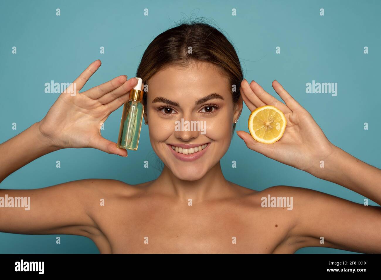 A young model holds a serum with vitamin c and half a lemon on a blue ...