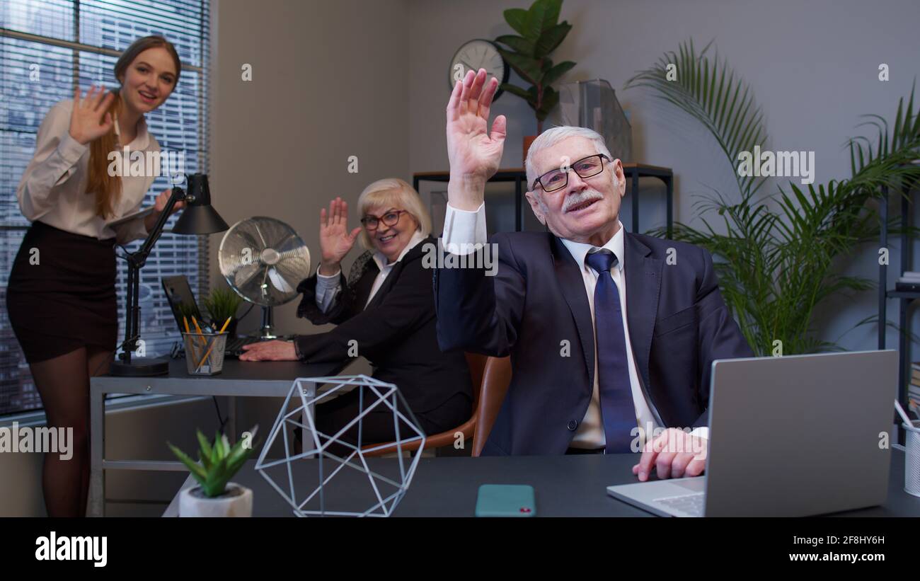 Senior businessman with colleagues team waves palm in hello gesture ...