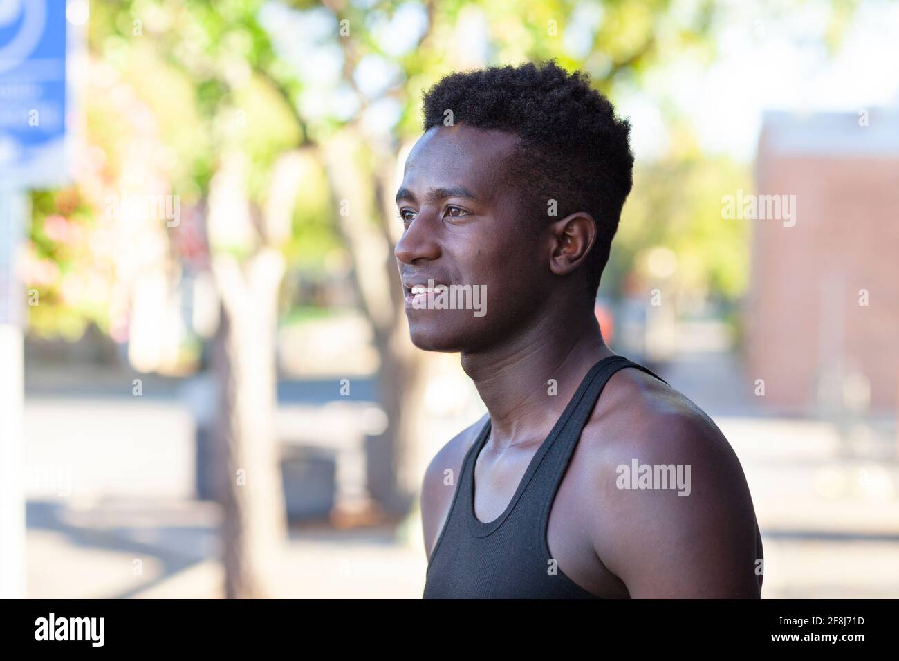 A handsome young black man stands in a street with defocused background ...