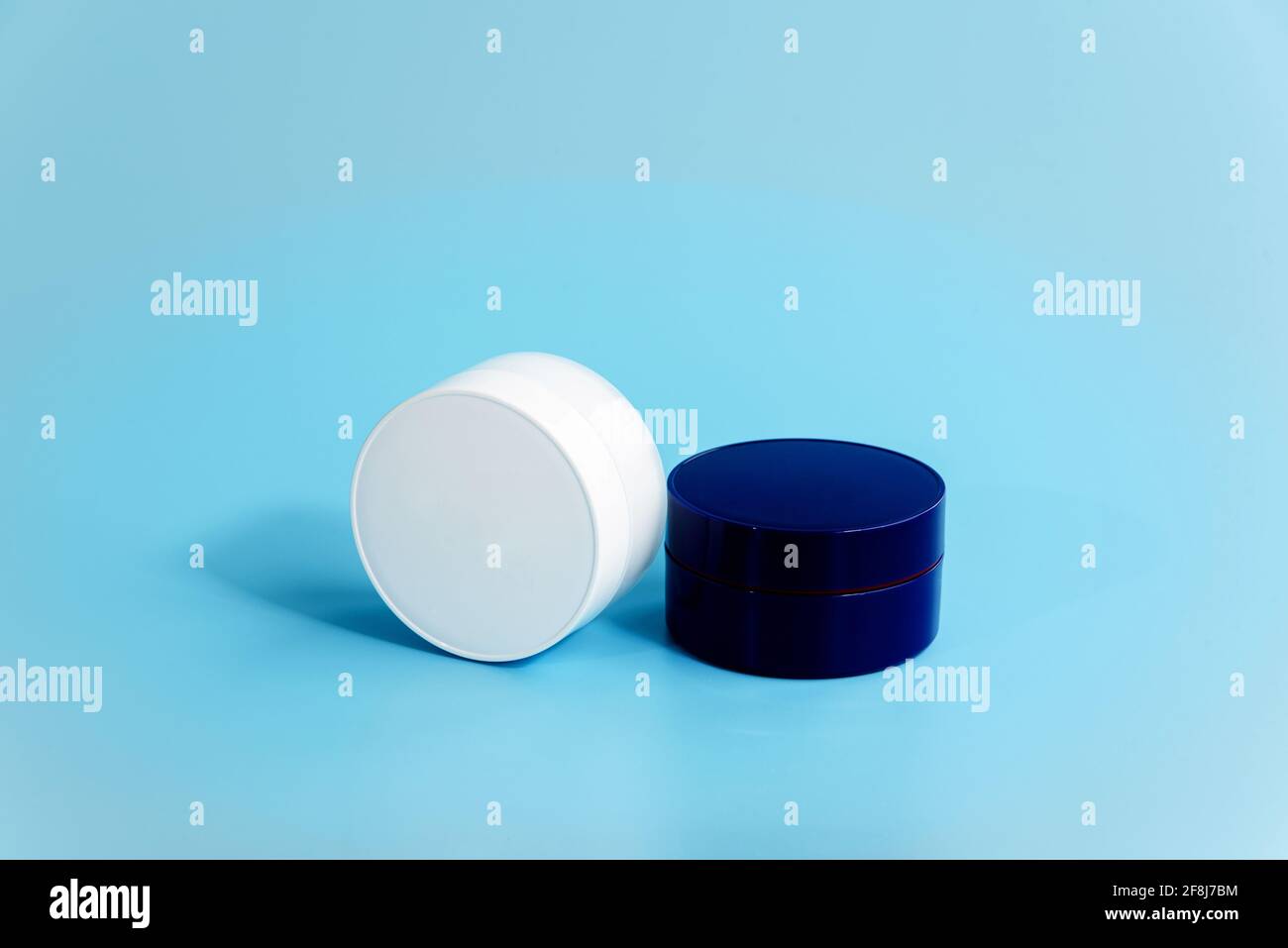 Two closed plastic cream jars on light blue background. Blank white and ...