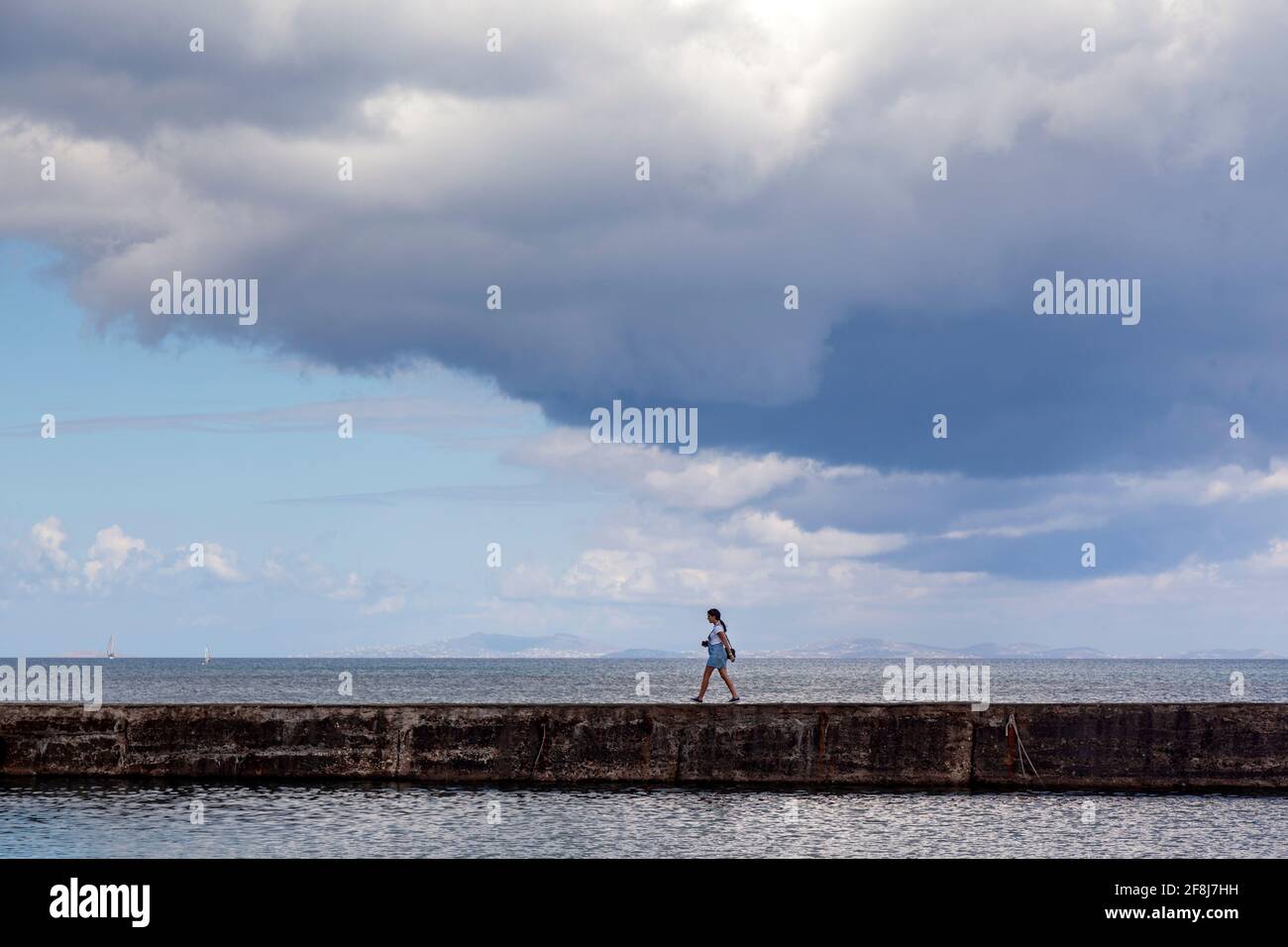A lonely girl walking upon a stone dock right by the sea during a heavy ...