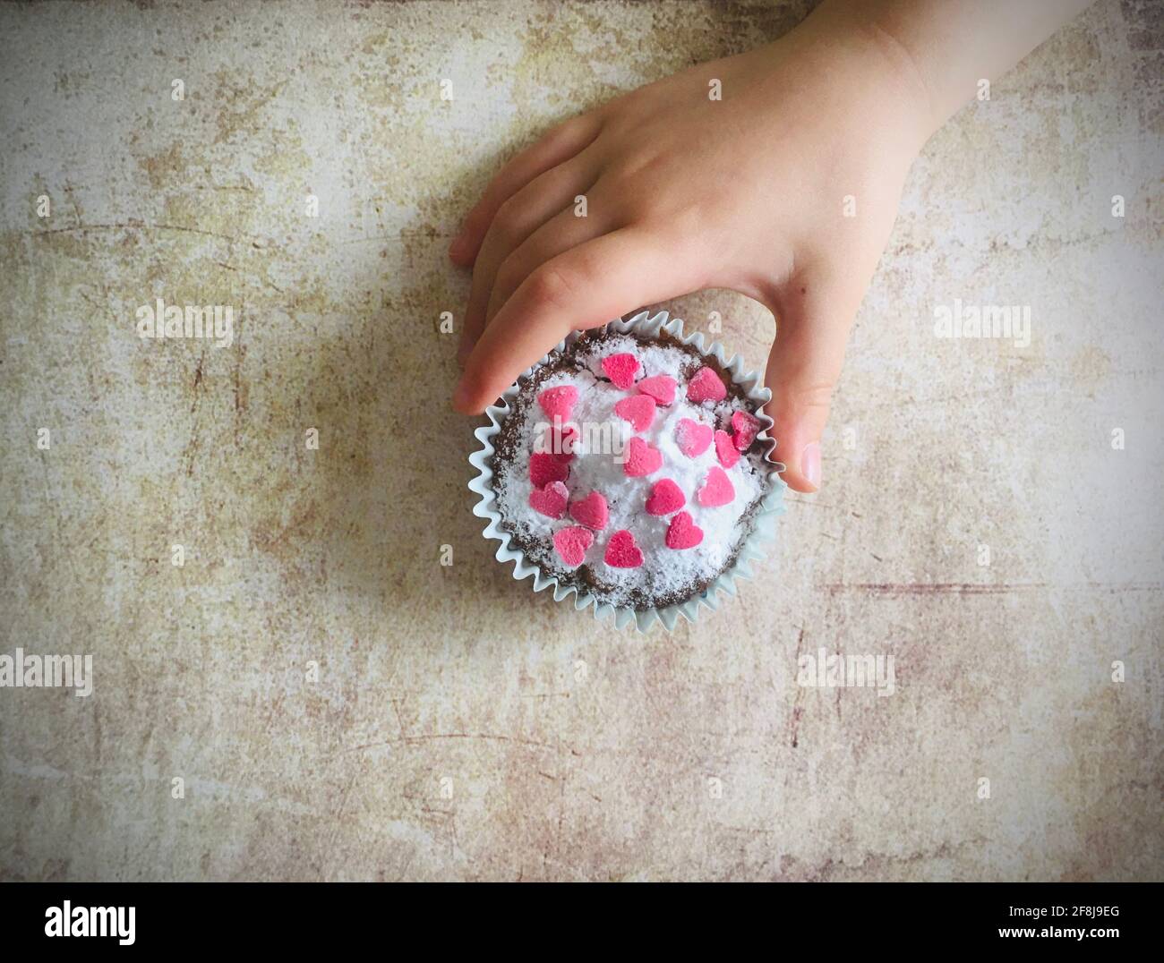 Overhead view of a child reaching for a chocolate cupcake with sugar ...