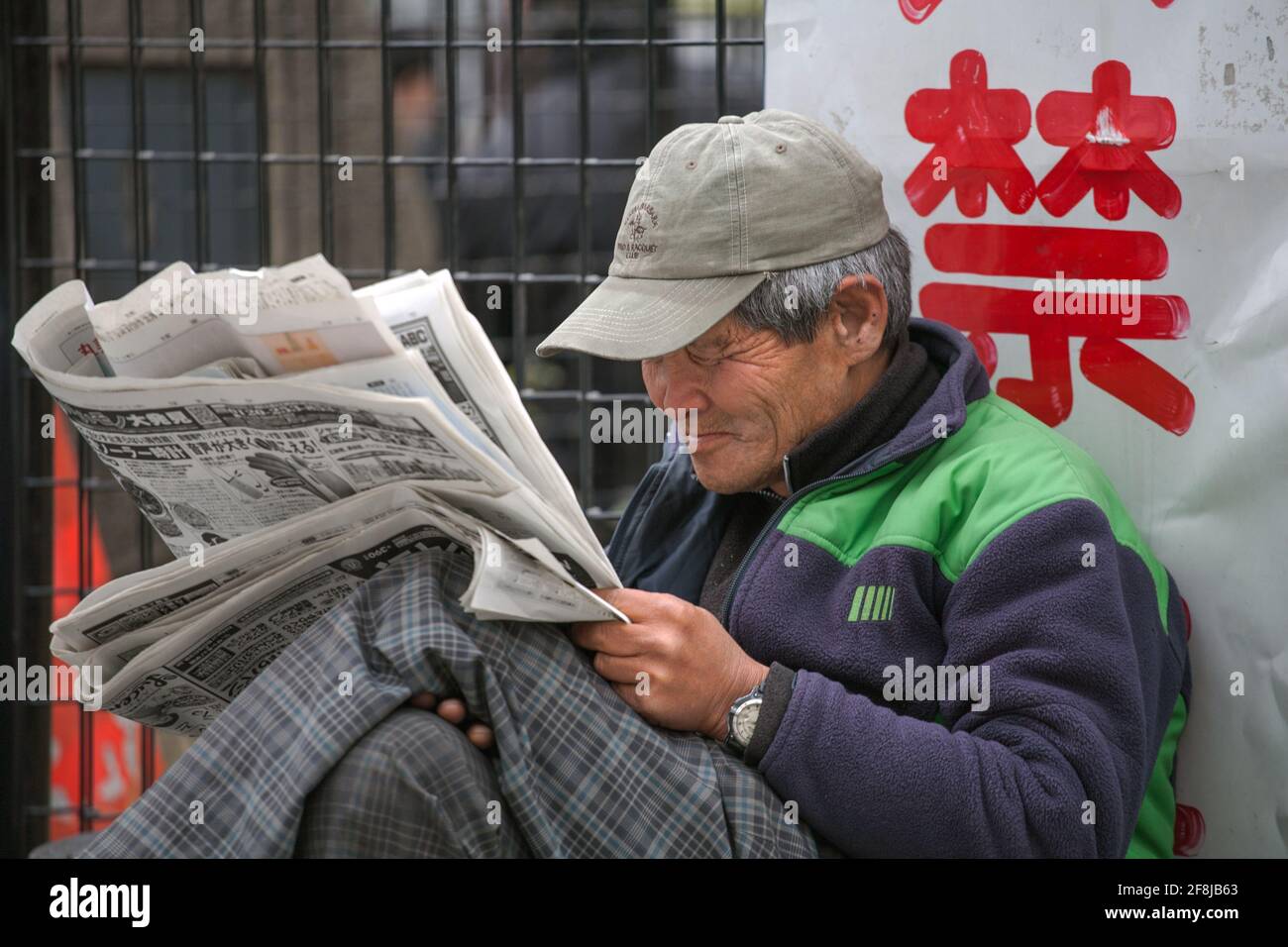 Homeless Japanese man sits reading newspaper on sidewalk, Shinjuku ...