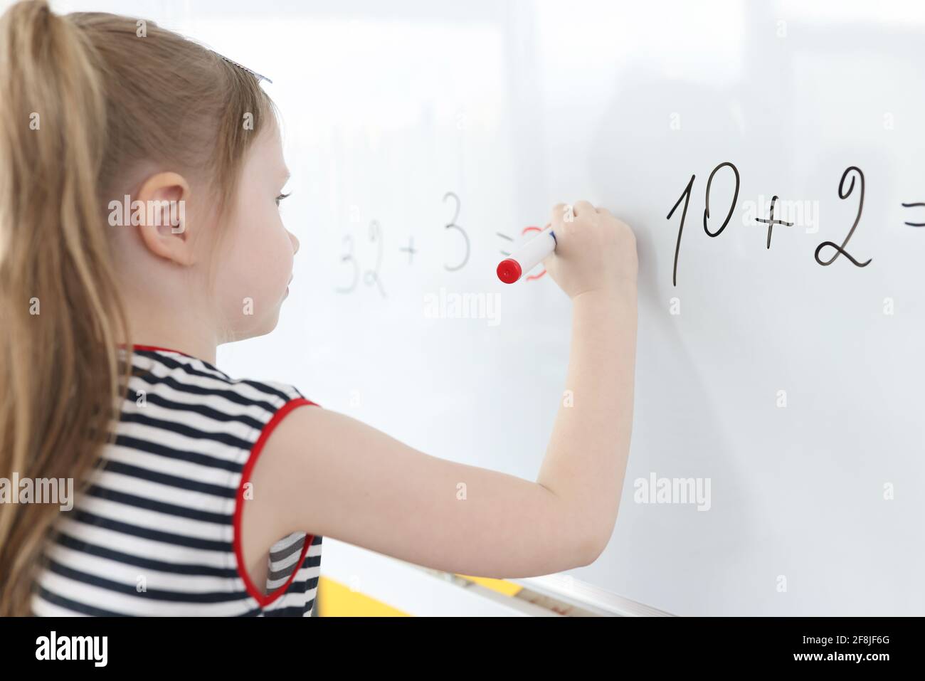 Little girl writes math examples on white board Stock Photo - Alamy