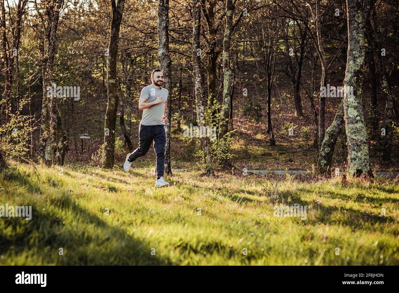 Man in cap and dark tracksuit running through the forest Stock Photo ...
