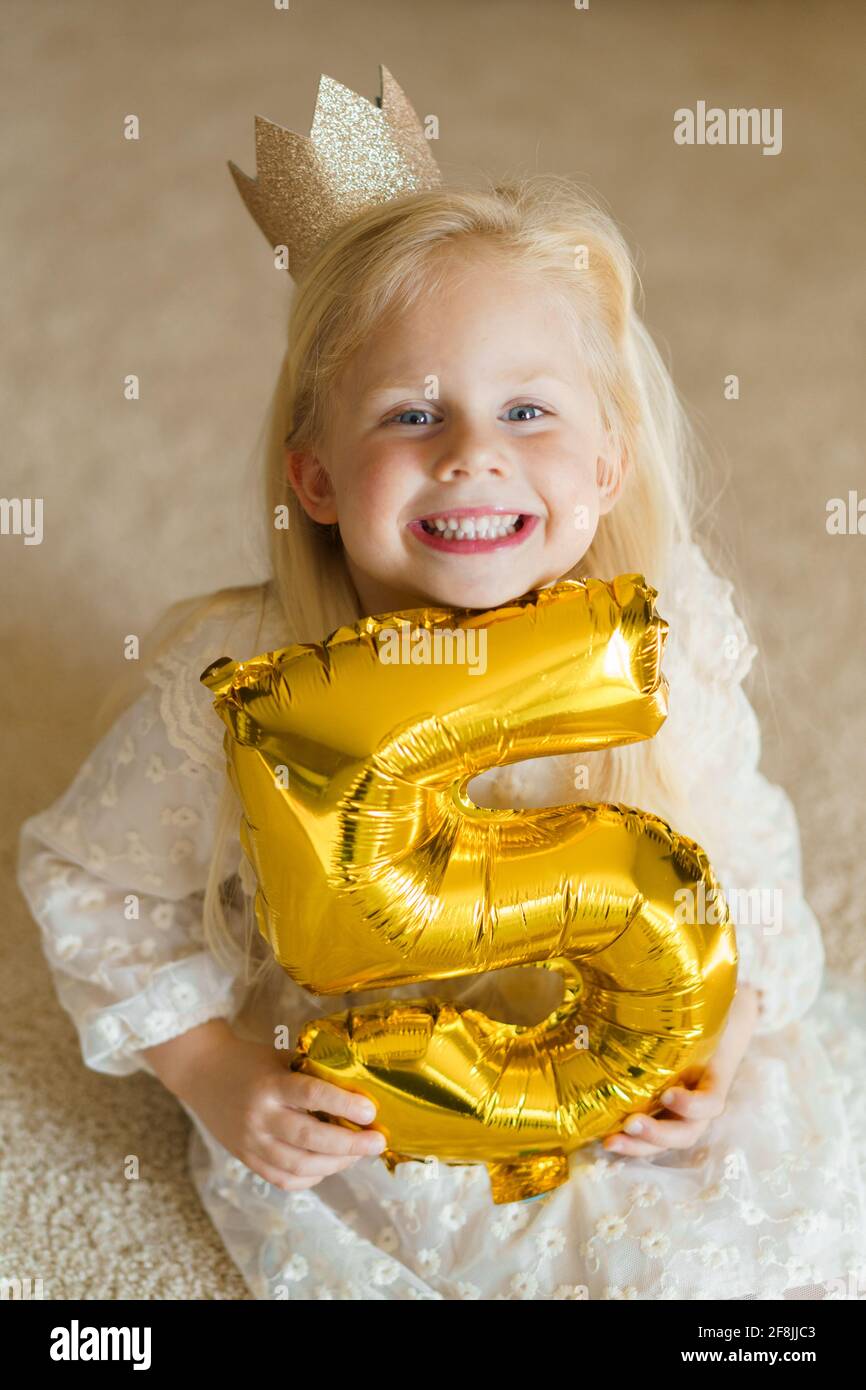 Happy smiling girl holding gold balloon number five Stock Photo - Alamy
