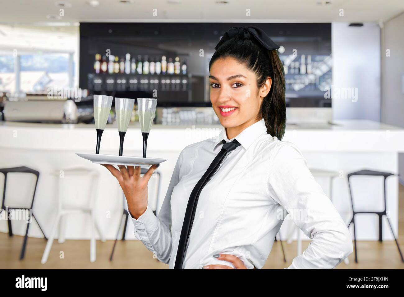 A girl waiter with three glasses of champagne on a white plate poses in ...