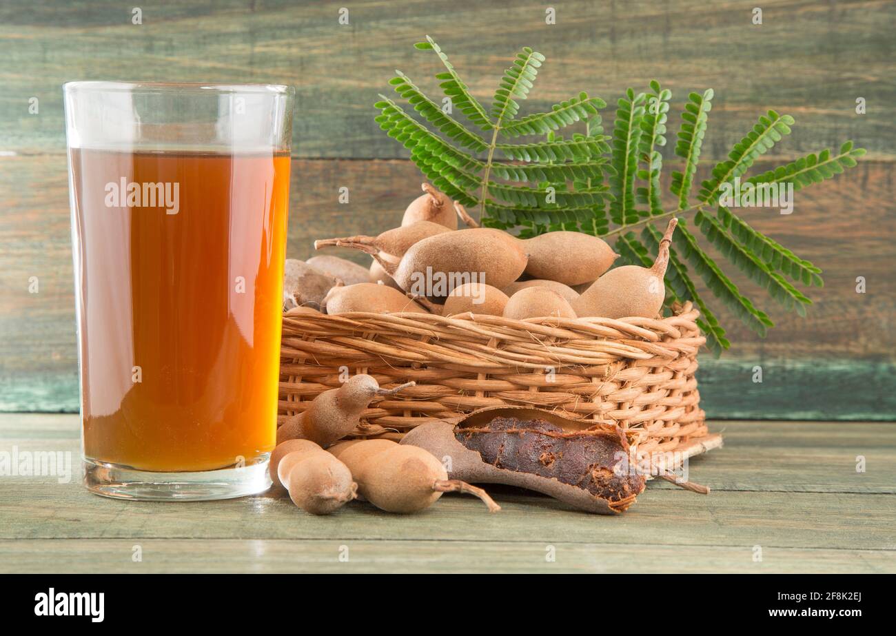 Tamarind juice in a glass surrounded by fresh ripe tamarinds ...