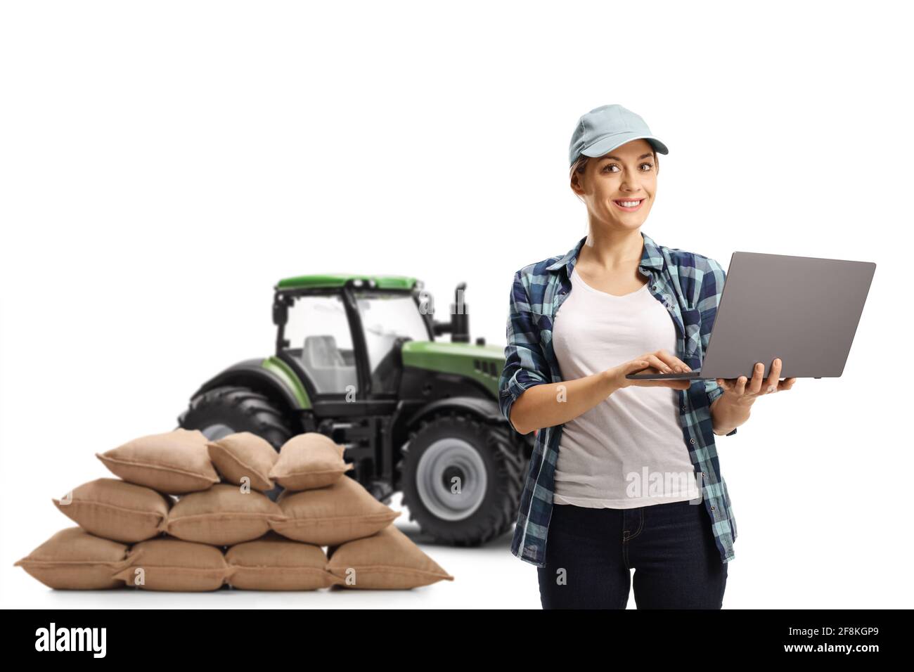 Female farmer holding a laptop computer and standing next to a pile od ...