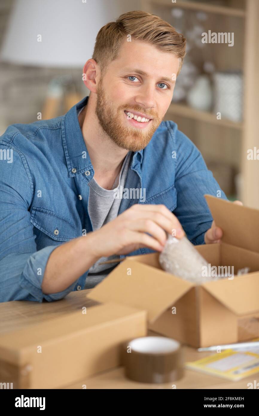young man in living room opening cardboard box package Stock Photo - Alamy