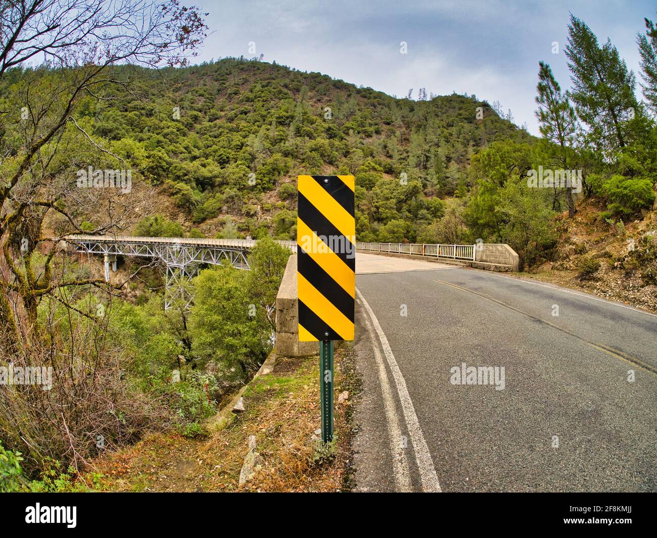 Closeup view of a Yellow and black caution sign in front of a bridge on ...
