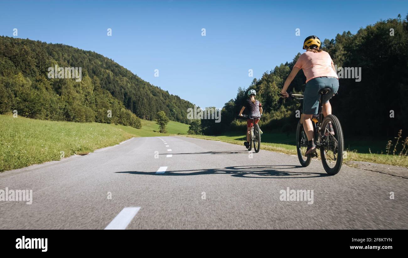 Woman and girl child riding mountain bikes on a country road in nature ...