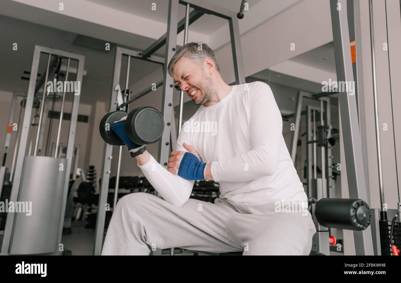 a man with a tense face lifts dumbbells while sitting on a bench in the ...